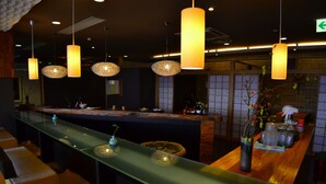 Uma área de bar moderna com um balcão comprido, luminárias pendentes e um vaso com flores.