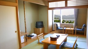 Quarto japonês tradicional com tatames, uma mesa de madeira baixa, televisão e vista para montanhas pela janela.