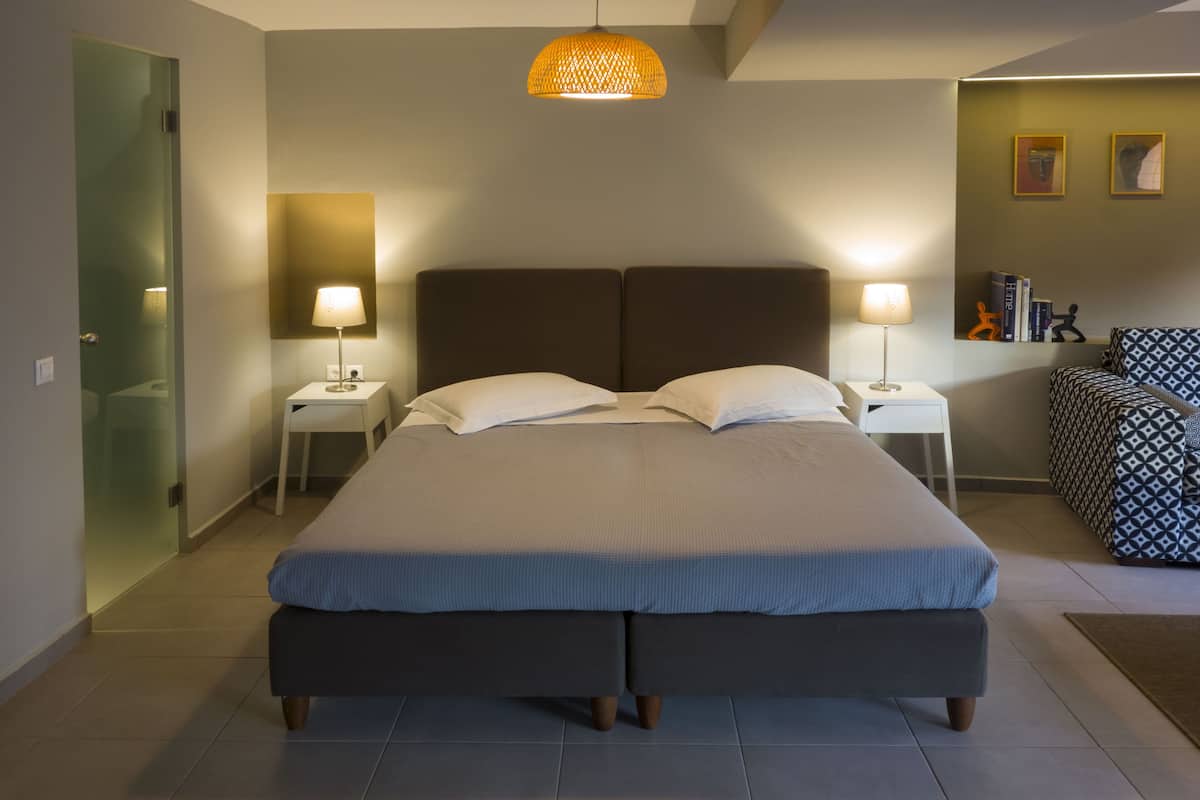 Quarto moderno com uma cama grande, duas mesas de cabeceira, um abajur e uma pequena estante.