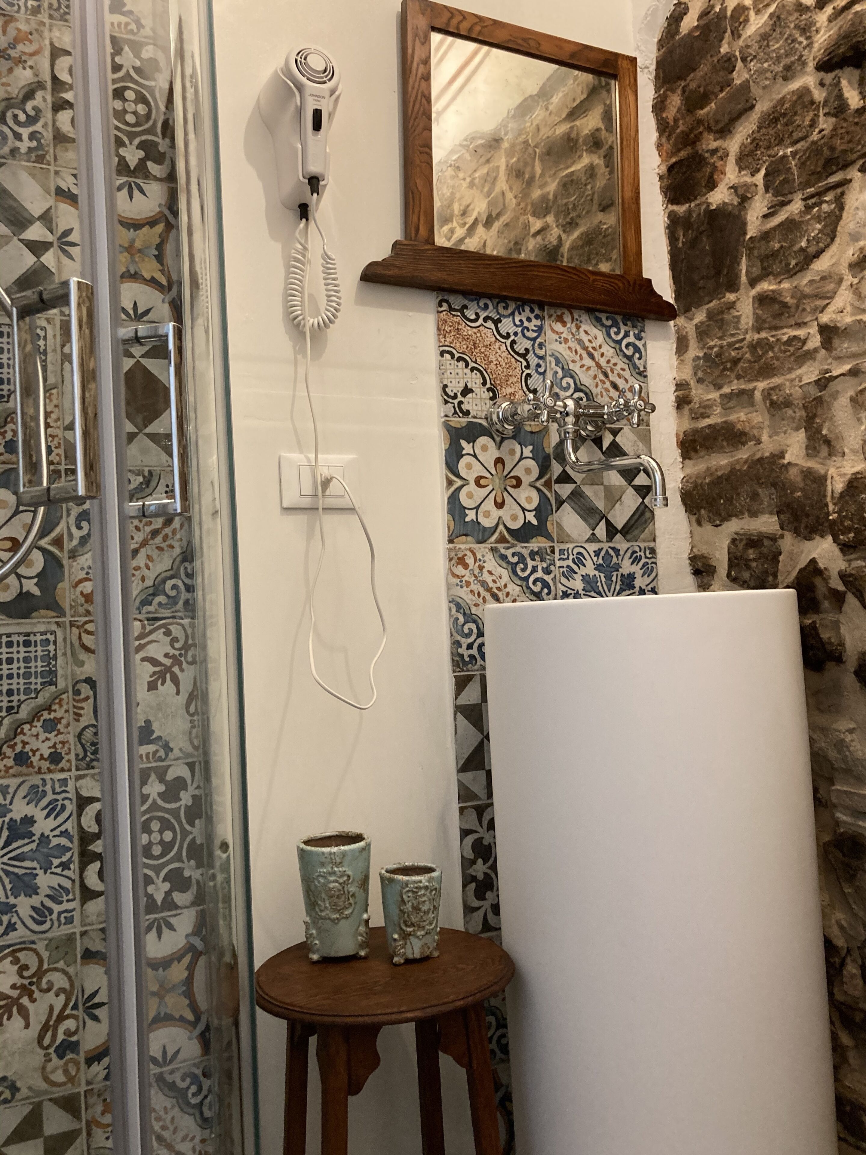 Casa de banho com azulejos estampados, secador de cabelo, espelho e uma pequena mesa com objetos decorativos.