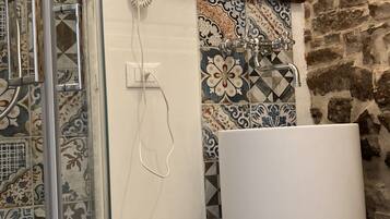 Casa de banho com azulejos estampados, secador de cabelo, espelho e uma pequena mesa com objetos decorativos.