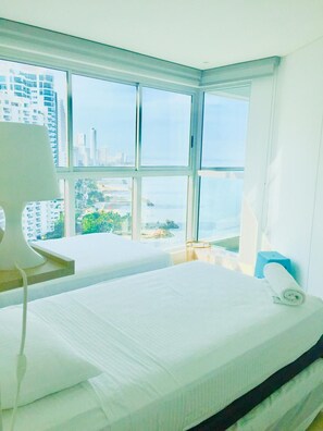 Quarto de hotel com duas camas, uma janela grande e vista para a paisagem urbana.
