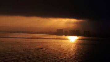 Um pôr do sol sobre a água, com o horizonte de uma cidade ao longe.