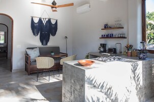 Uma cozinha moderna com uma ilha central, uma área de jantar com sofá e cadeiras, e um ventilador de teto.