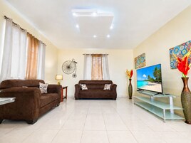 Uma sala de estar com dois sofás marrons, uma televisão e um ventilador fixado na parede.