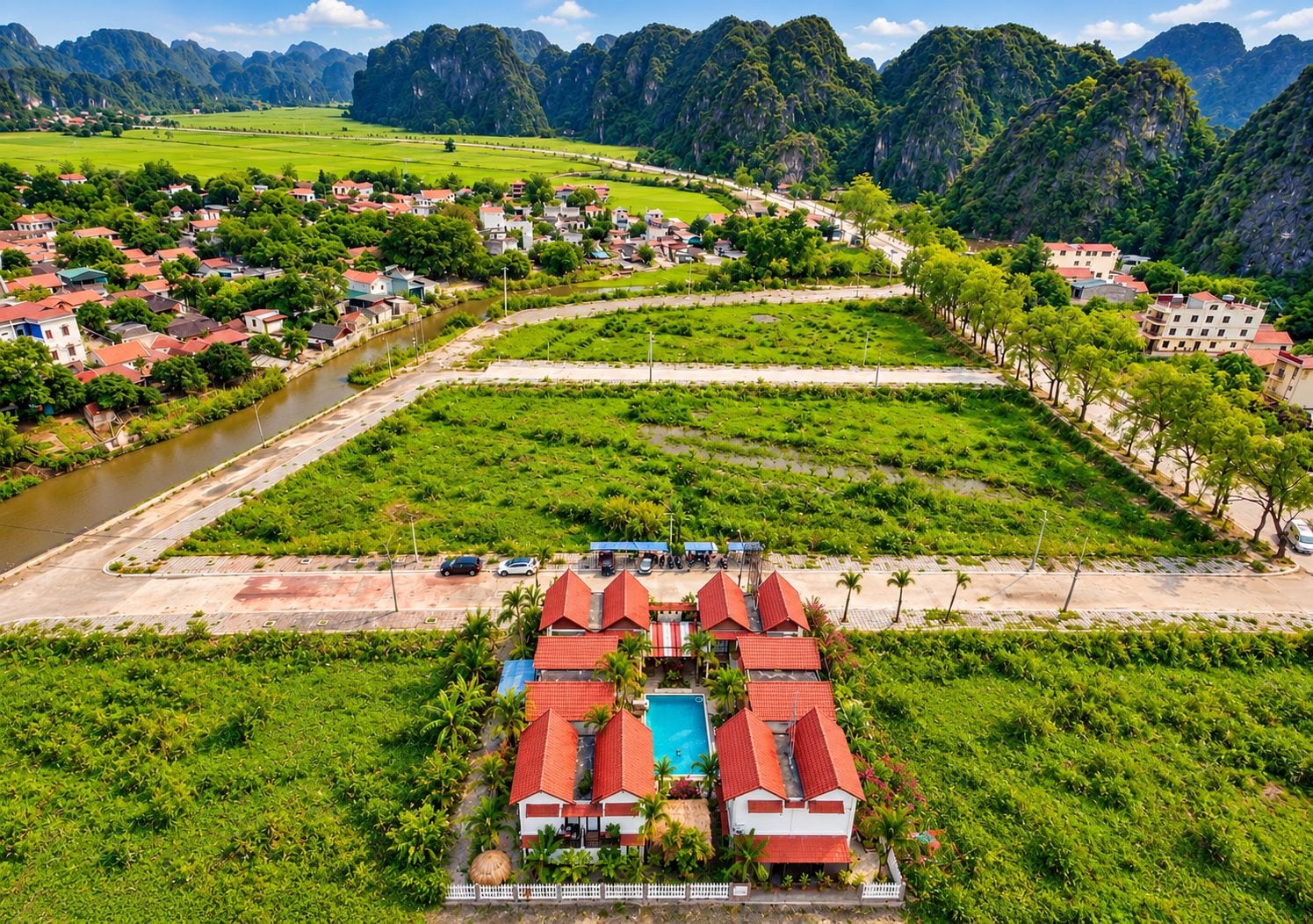 Vista aérea de uma área residencial com um edifício central com piscina, cercado por vegetação exuberante e um rio.