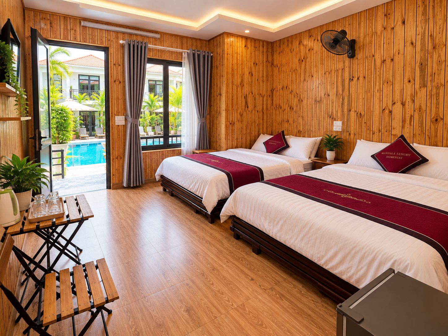 Quarto de hotel com duas camas, paredes de madeira, vista para a piscina e uma mesa com copos.