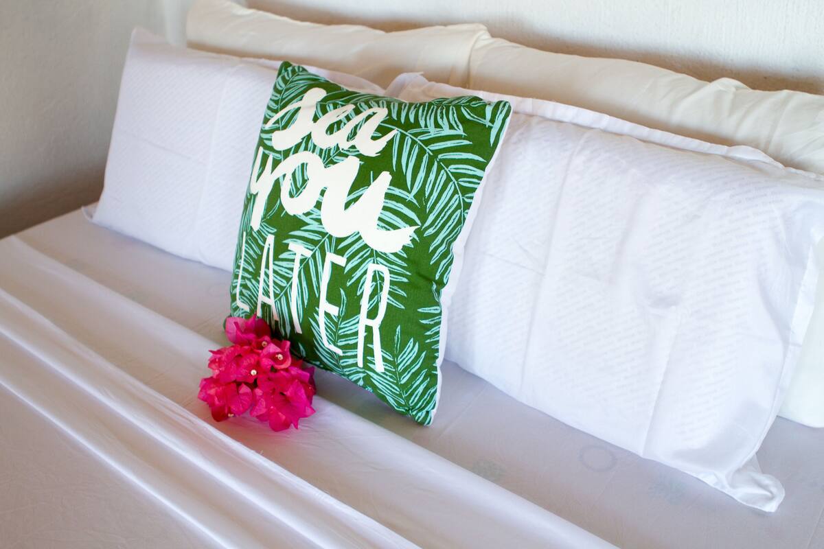 Cama com roupa de cama branca e travesseiro verde com texto branco.