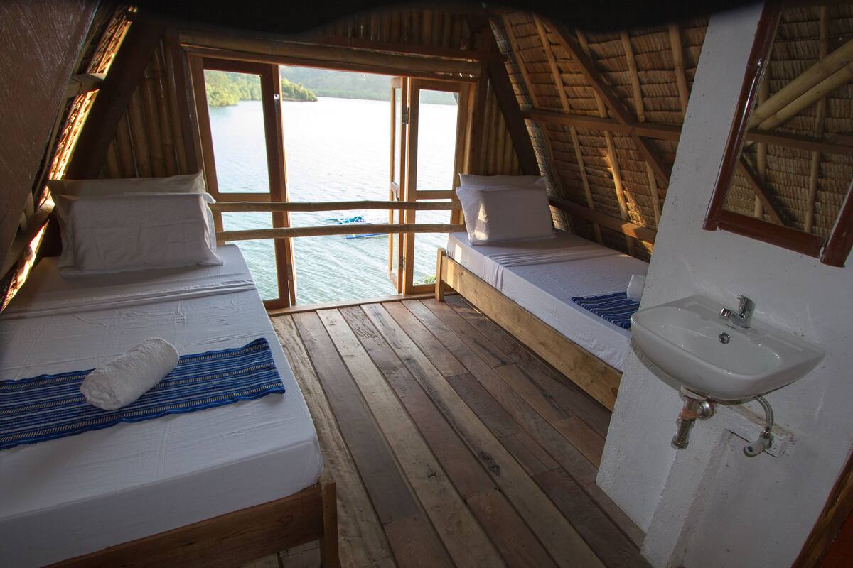 Uma cabana com duas camas, piso de madeira, janela com vista para a água e uma pia.