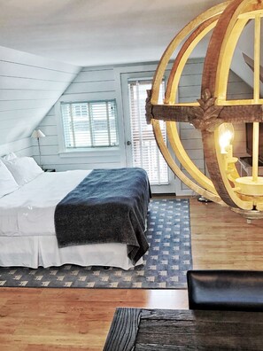Quarto com teto inclinado, cama com roupa de cama branca, tapete azul estampado e piso de madeira.