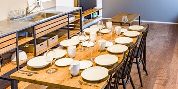 Uma área de refeições com várias mesas preparadas para o serviço, equipadas com pratos, copos e talheres.