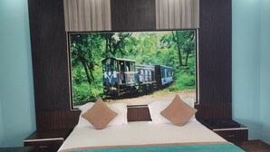 Quarto com uma cama grande, duas mesas de cabeceira e uma televisão exibindo uma cena de trem.