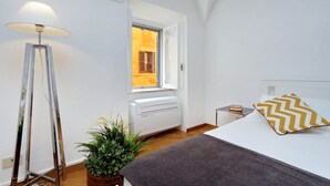 Quarto com cama, mesa de cabeceira, luminária, planta em vaso e janela com vista.