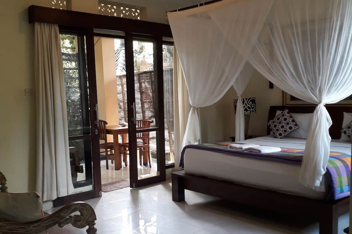 Quarto com cama, uma cadeira e porta de vidro deslizante para área externa.