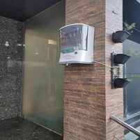 Casa de banho moderna com cabine de duche em vidro, secador de mãos embutido na parede e planta em vaso.