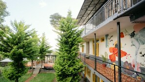 Um edifício com varanda, um mural com pássaros e flores, e um jardim com árvores e um caminho.