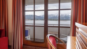 Quarto com uma grande porta de vidro deslizante que dá para uma vista do lago, uma cadeira vermelha e uma mesa de madeira.