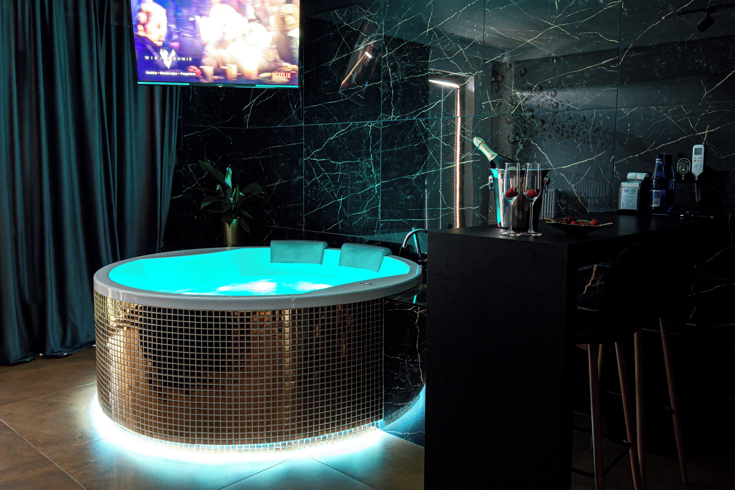 Casa de banho moderna com hidromassagem, uma televisão na parede e zona de bar com taburetes.