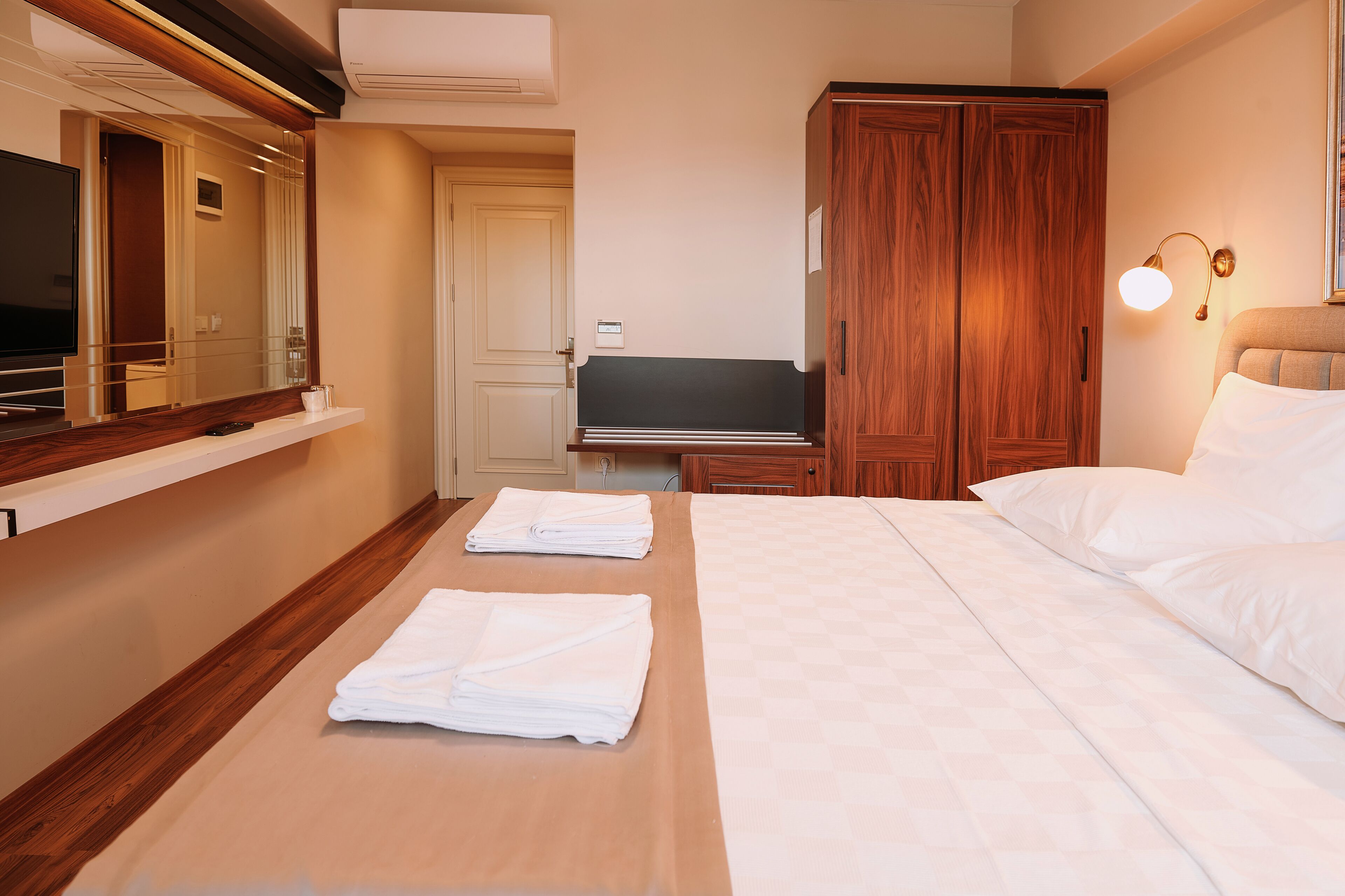 Quarto de hotel com cama, televisão, guarda-roupa e casa de banho visível através de uma porta aberta.