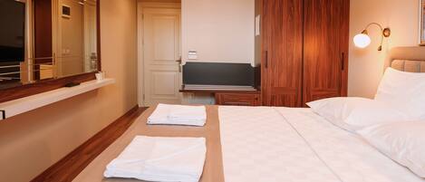 Quarto de hotel com cama, televisão, guarda-roupa e casa de banho visível através de uma porta aberta.