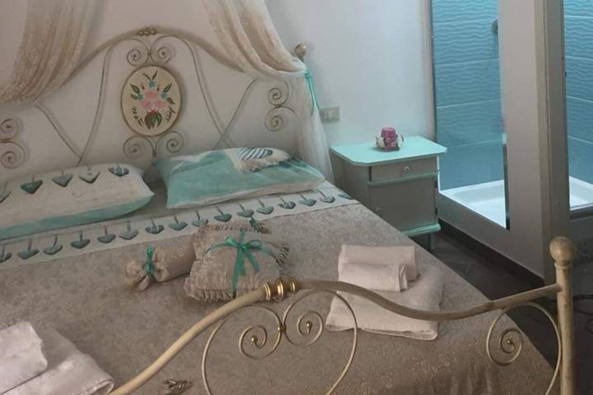 Quarto com cama, mesa de cabeceira, luminária e uma janela com persianas.