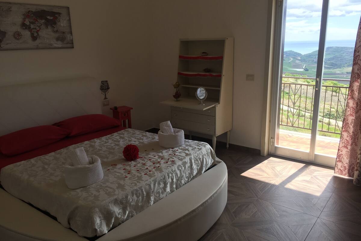 Quarto com cama, cômoda, espelho e vista para o exterior.