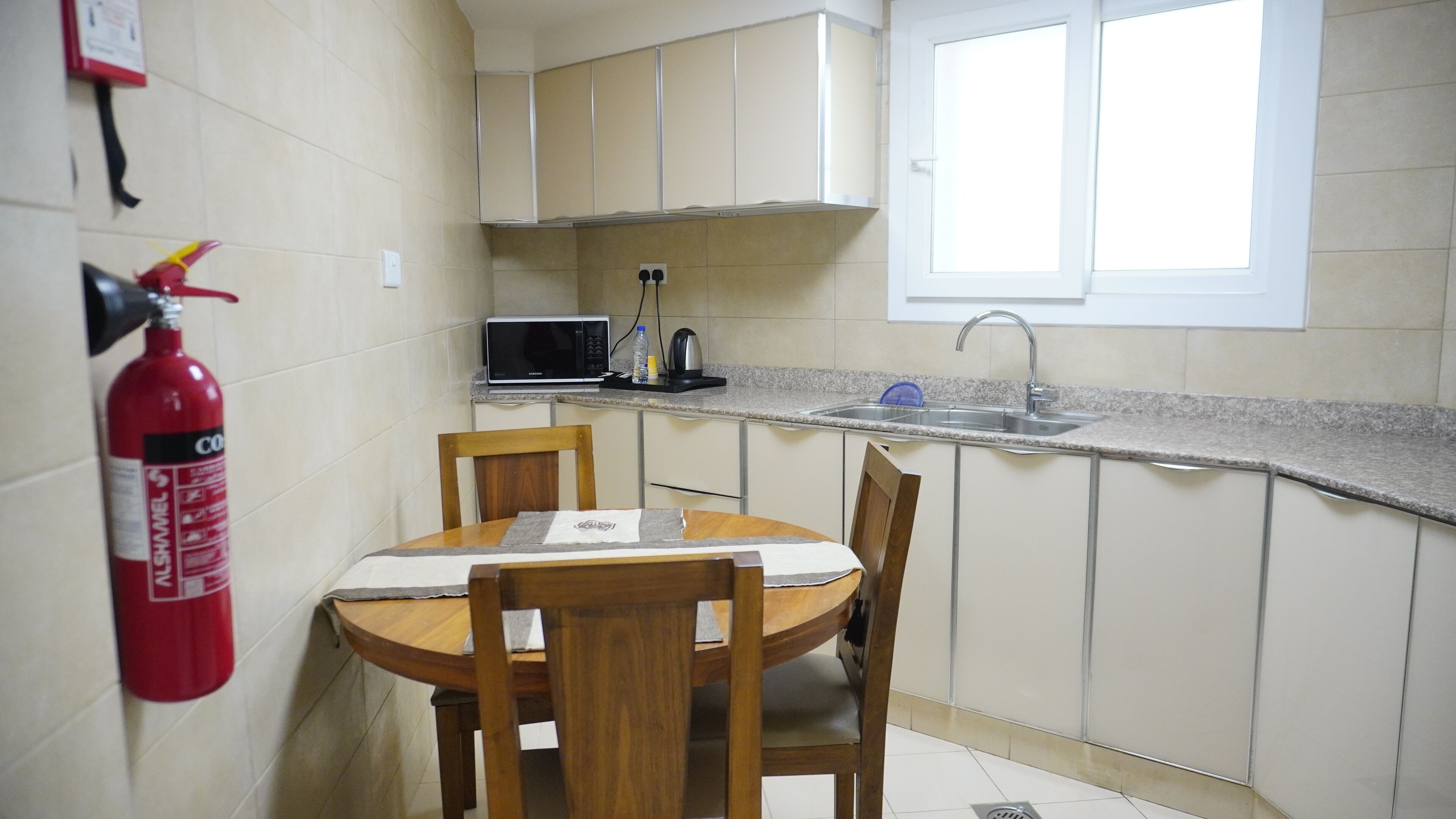 Uma cozinha compacta com uma mesa de jantar e cadeiras, micro-ondas, pia e uma janela.