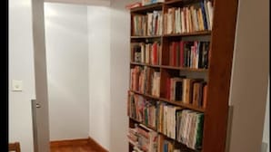 Um corredor com piso de madeira, uma estante cheia de livros e uma cadeira.