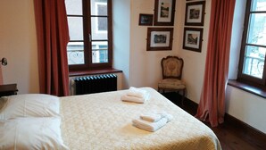 Cama bem arrumada com toalhas dobradas, um radiador, uma cadeira e quadros nas paredes.