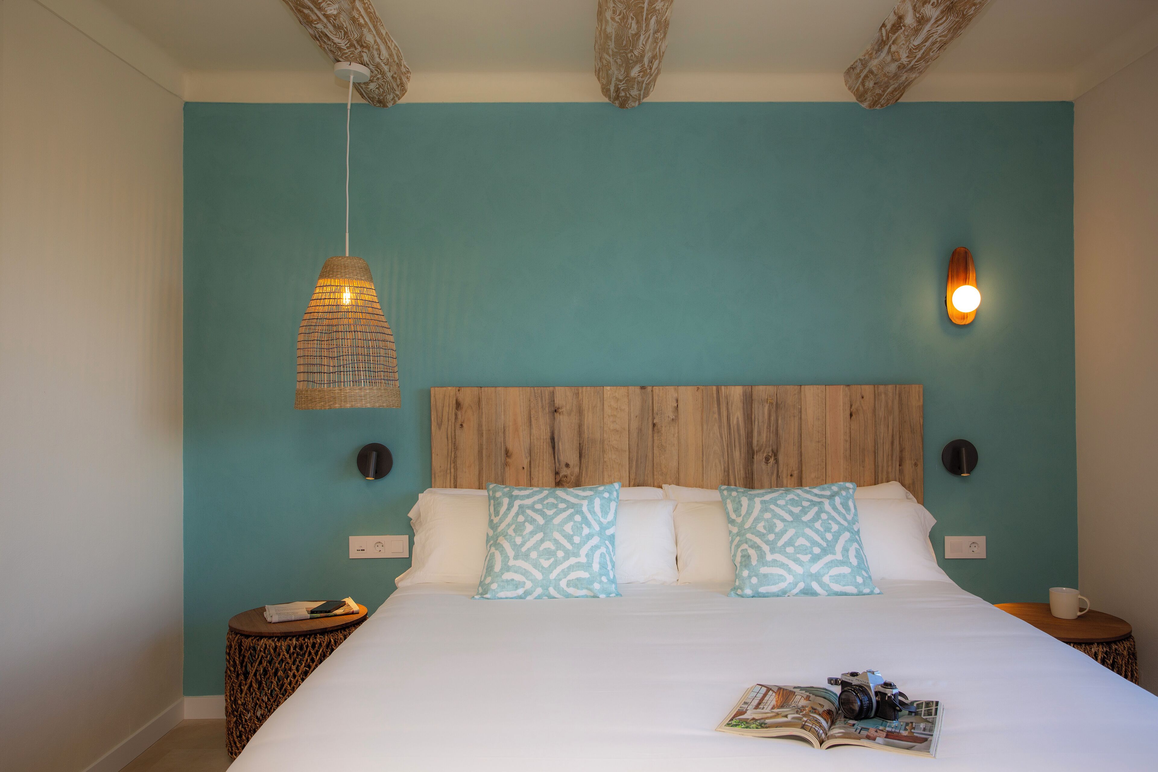 Cama bem arrumada com almofadas estampadas, luminária pendente e luminária na parede.