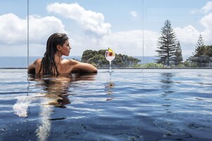Uma pessoa em uma piscina com vista clara para o oceano e árvores ao fundo.