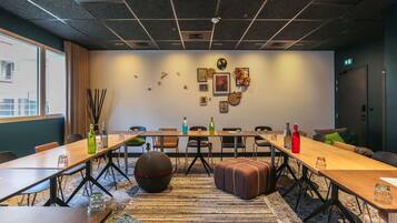 Uma sala de conferências com uma mesa comprida, cadeiras, um banquinho redondo e um tapete estampado.