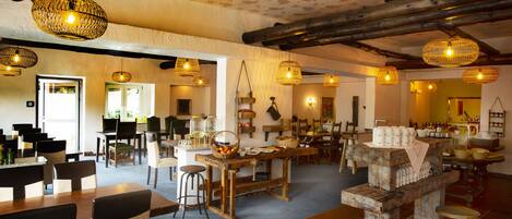 Um restaurante amplo, com mesas e cadeiras de madeira, lustres de vime suspensos e teto rústico.
