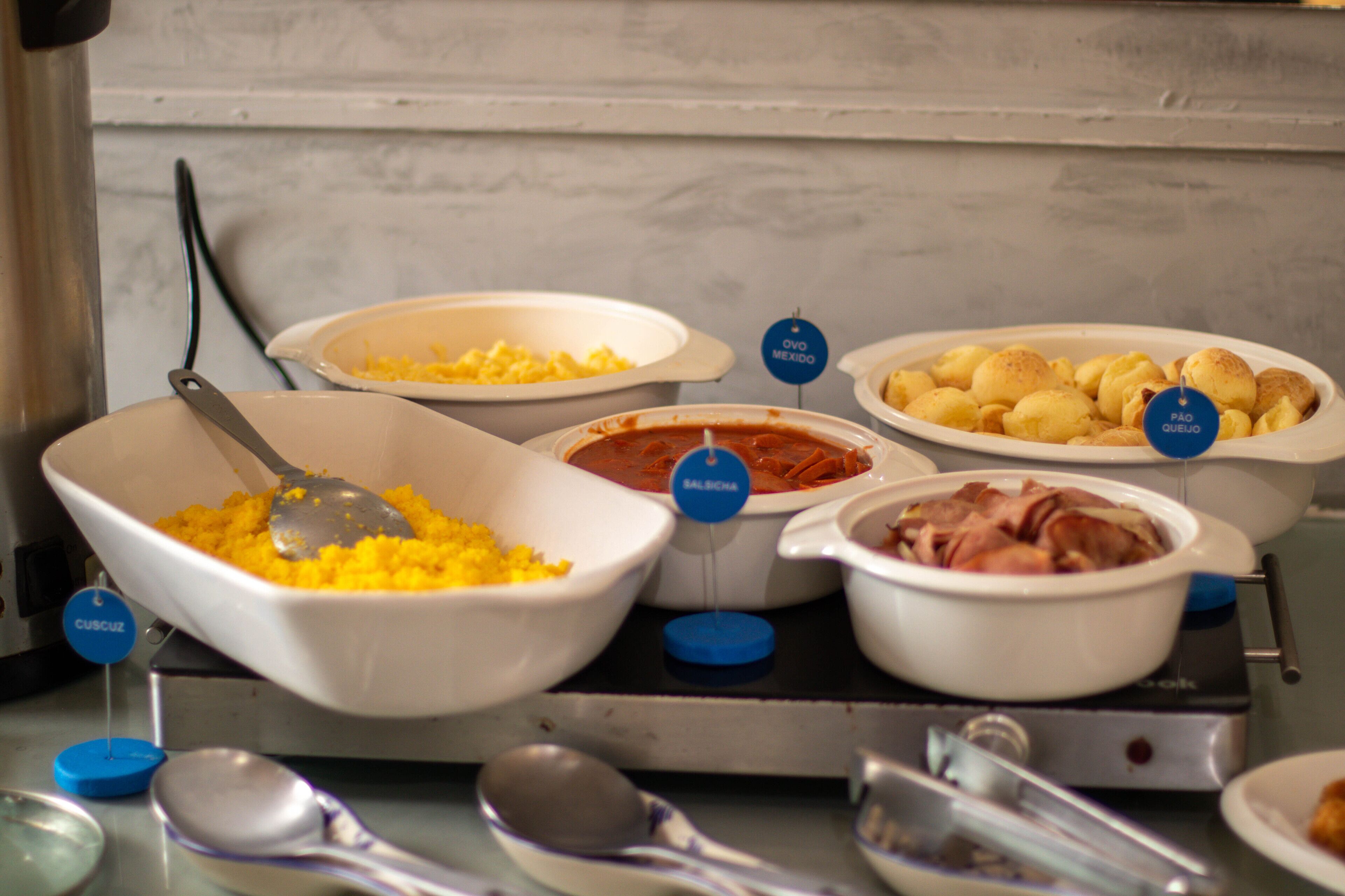 Buffet com pratos identificados, incluindo ovos mexidos, salsa e presunto.