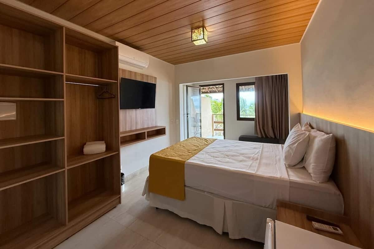 Quarto com cama, guarda-roupa de madeira e televisão.