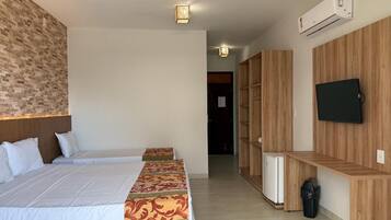 Quarto de hotel com duas camas, televisão, guarda-roupa de madeira e uma pequena cozinha.