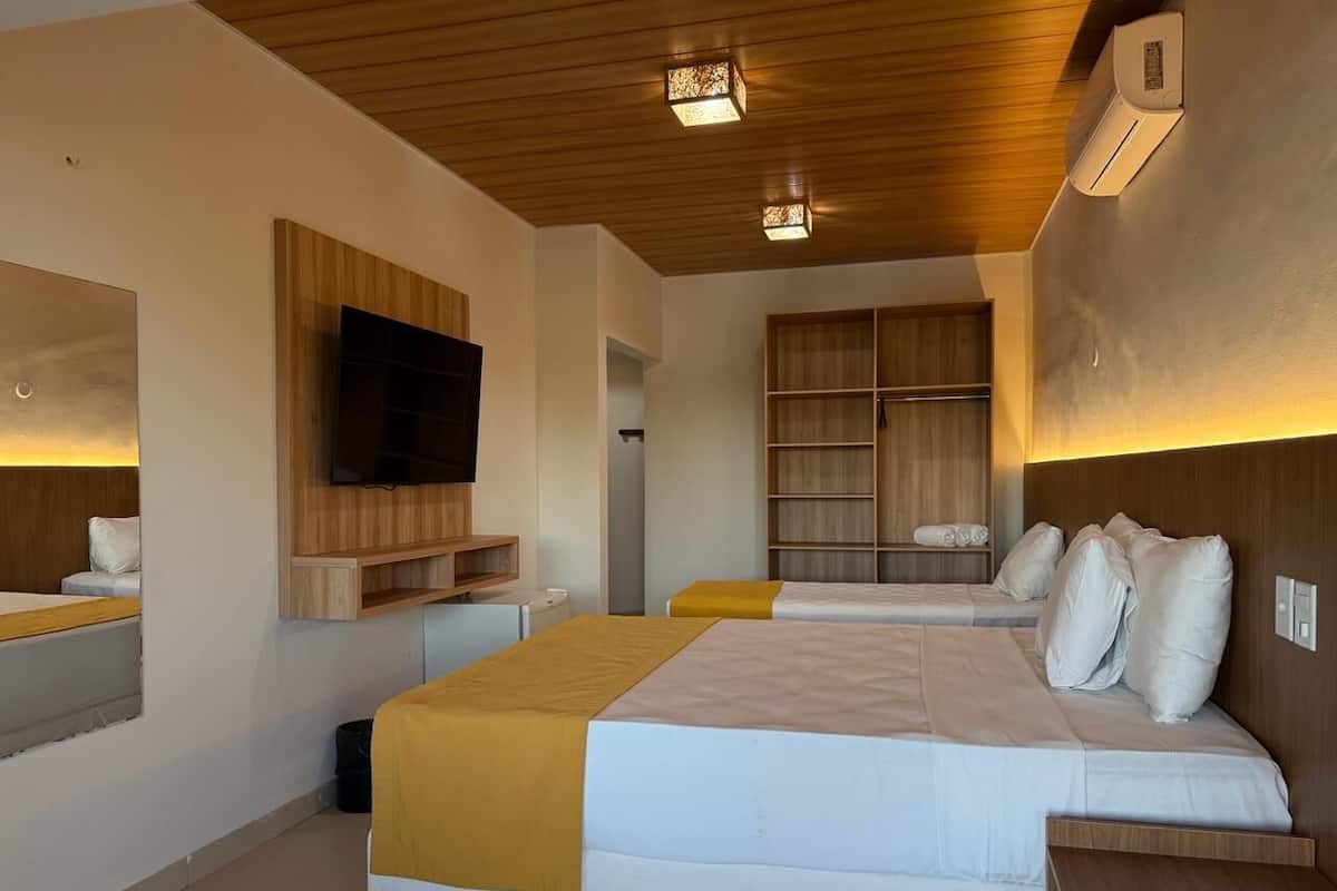 Quarto de hotel moderno com uma cama grande, televisão fixada na parede e roupeiro embutido.