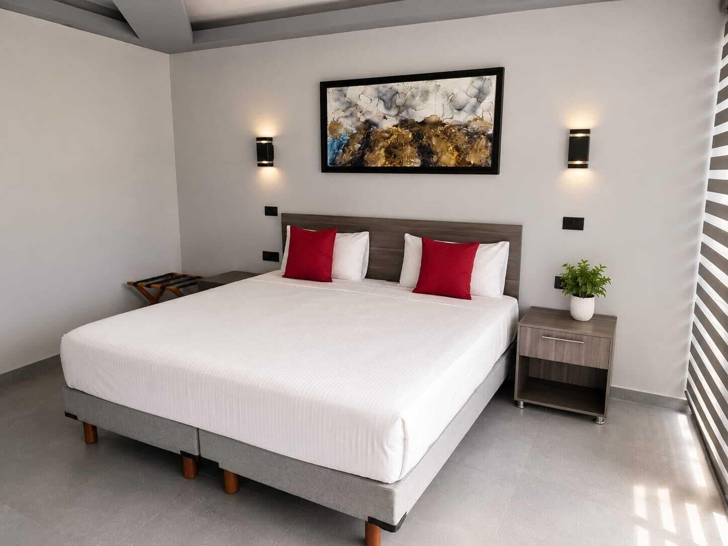 Quarto moderno com uma cama grande, duas mesas de cabeceira, um quadro na parede e um vaso de planta.