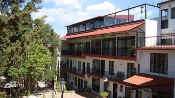 Um edifício com várias andares, varandas e janelas amplas, rodeado por árvores e um céu claro.