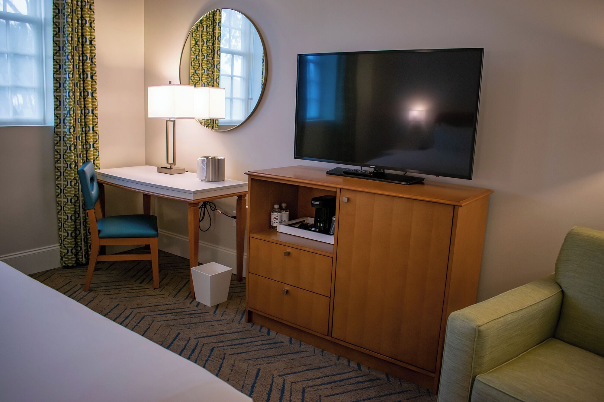 Quarto de hotel com escrivaninha, cadeira, televisão e armário.