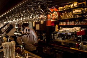 Uma área de bar com uma fileira de copos de vinho pendurados e um bartender preparando bebidas.