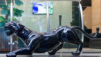 Estátua de uma pantera negra em um saguão com portas de vidro, uma planta e uma tela digital ao fundo.