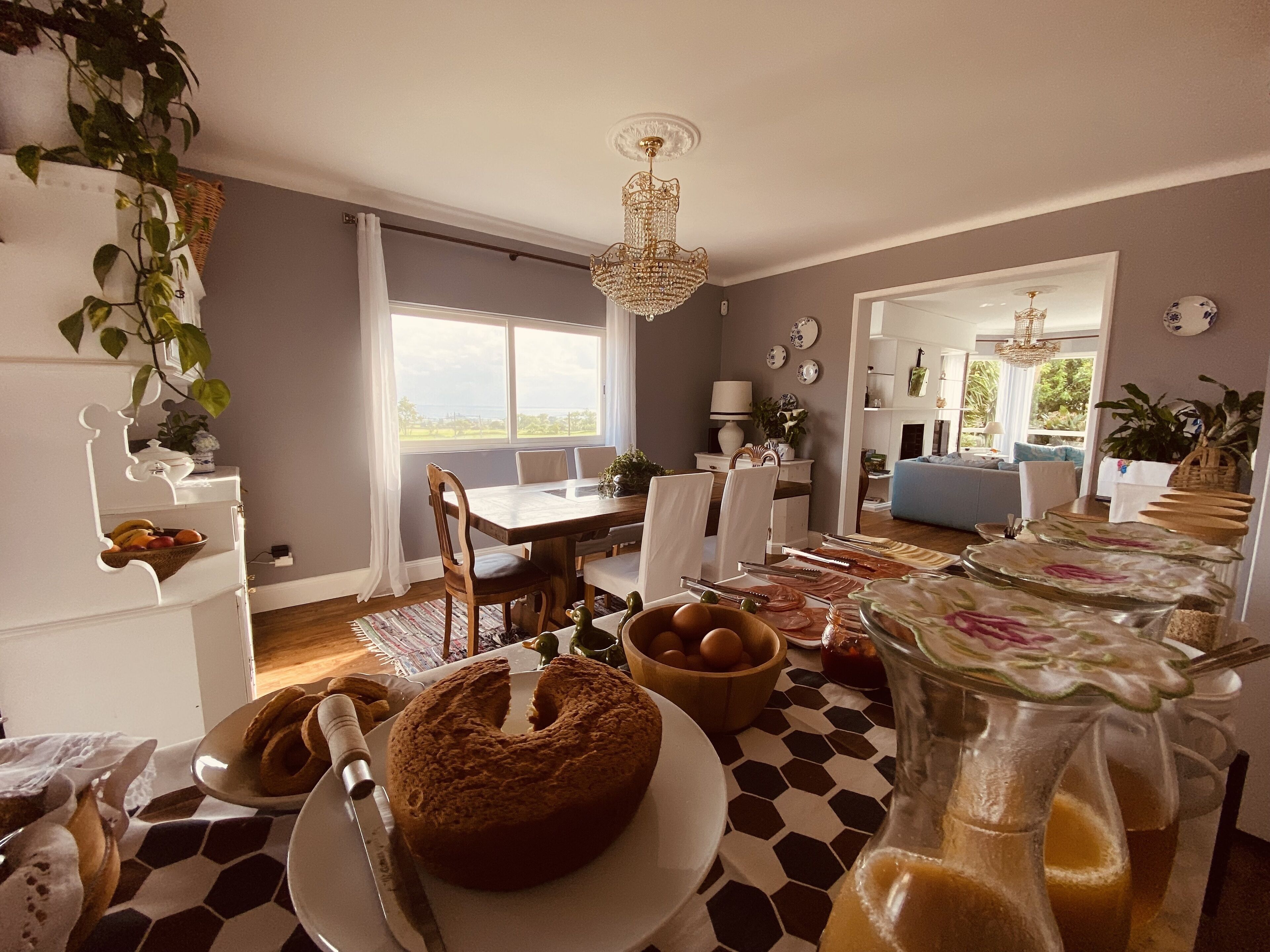 Uma sala de jantar com uma mesa grande, cadeiras, um candelabro e vista para o exterior.