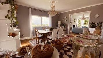 Uma sala de jantar com uma mesa grande, cadeiras, um candelabro e vista para o exterior.