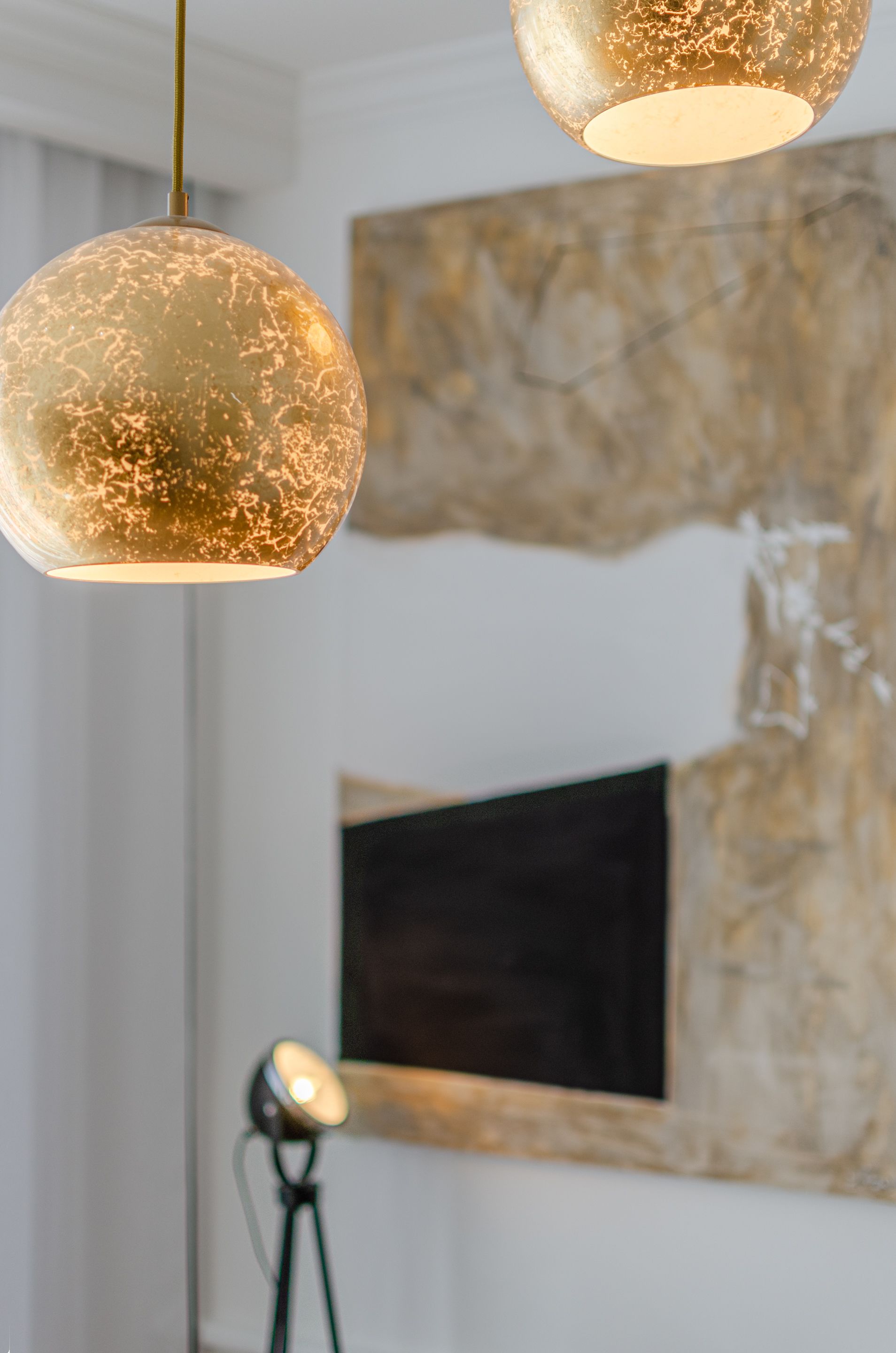 Um interior moderno com duas luminárias pendentes esféricas, um quadro abstrato emoldurado e um abajur com tripé.