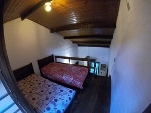 Um quarto pequeno e rústico com duas camas de madeira, teto inclinado e uma janela.