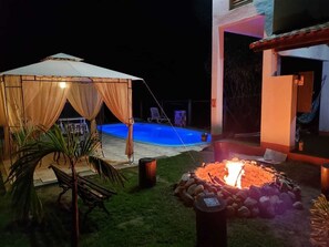 Um quintal com piscina, uma barraca e um espaço para fogueira.