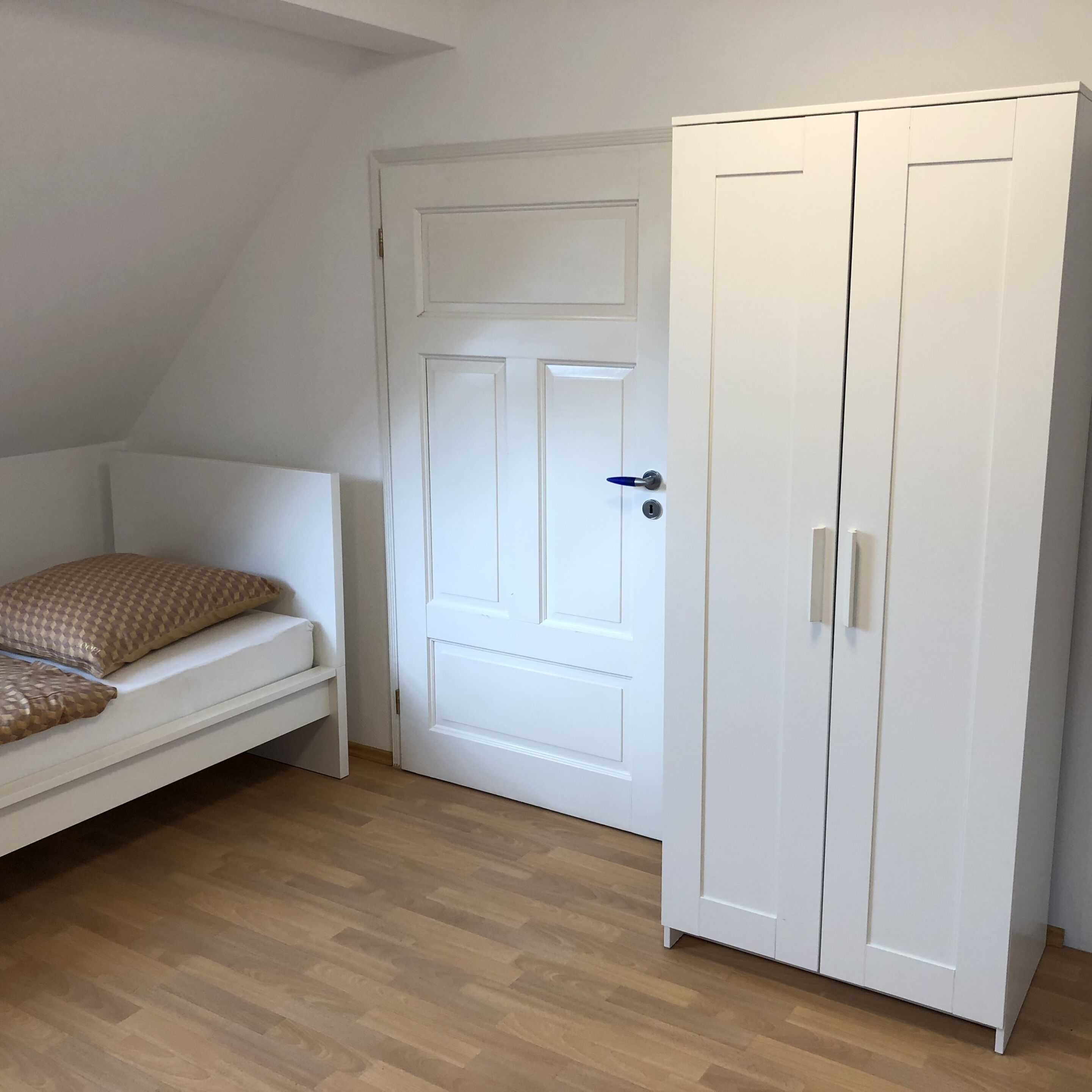 Quarto com uma cama branca, um guarda-roupa branco e uma porta branca.