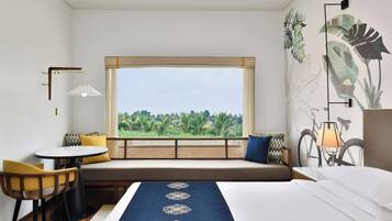 Quarto de hotel com uma janela grande, uma cama, um sofá, uma mesinha e uma cadeira.