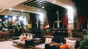 Uma área de estar acolhedora com móveis de vime, um palco para apresentações e uma grande janela com cortinas.